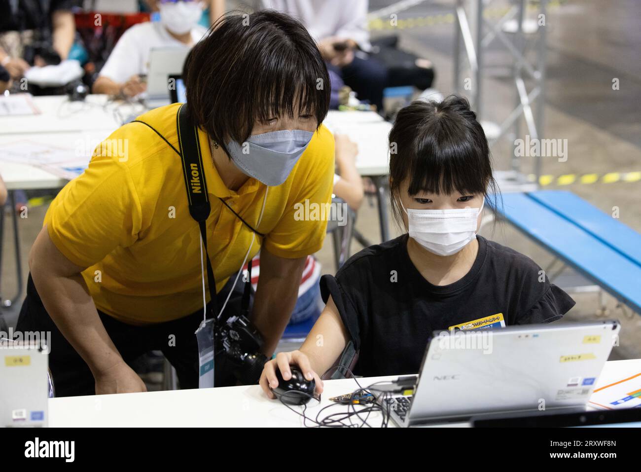 Participant of a video game programming workshop for kids receives help from an assistant inside ...