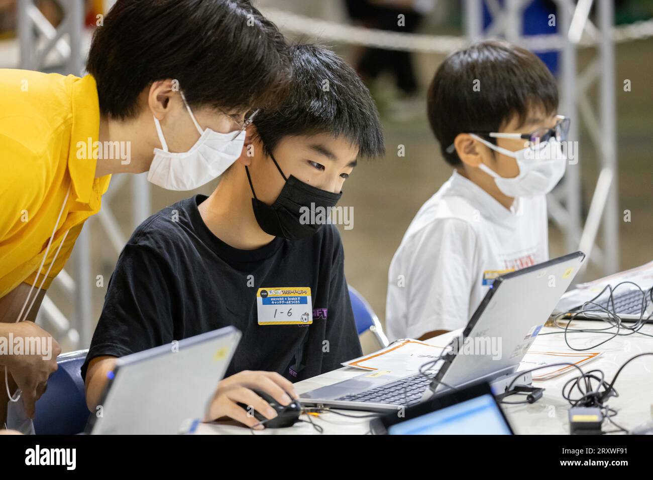 Participant of a video game programming workshop for kids receives help from an assistant inside ...