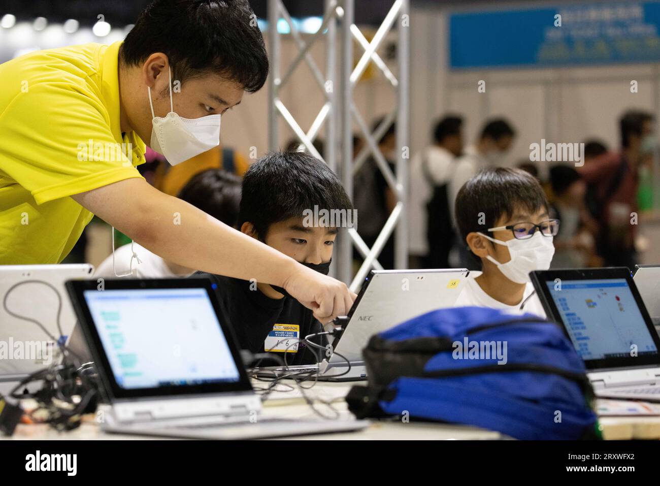 Participant of a video game programming workshop for kids receives help from an assistant inside ...