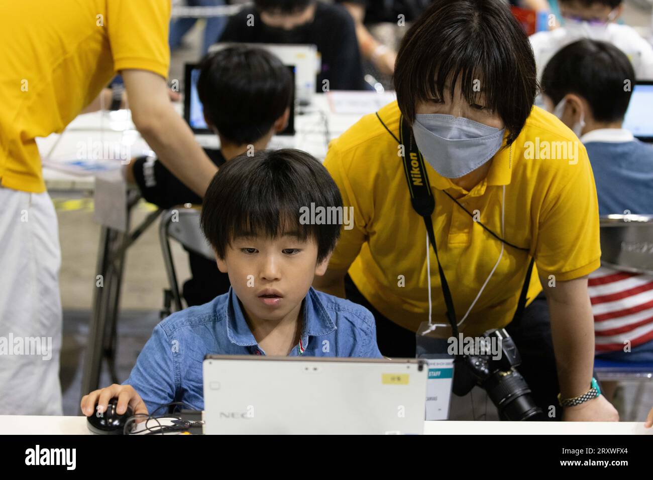 Participant of a video game programming workshop for kids receives help from an assistant inside ...