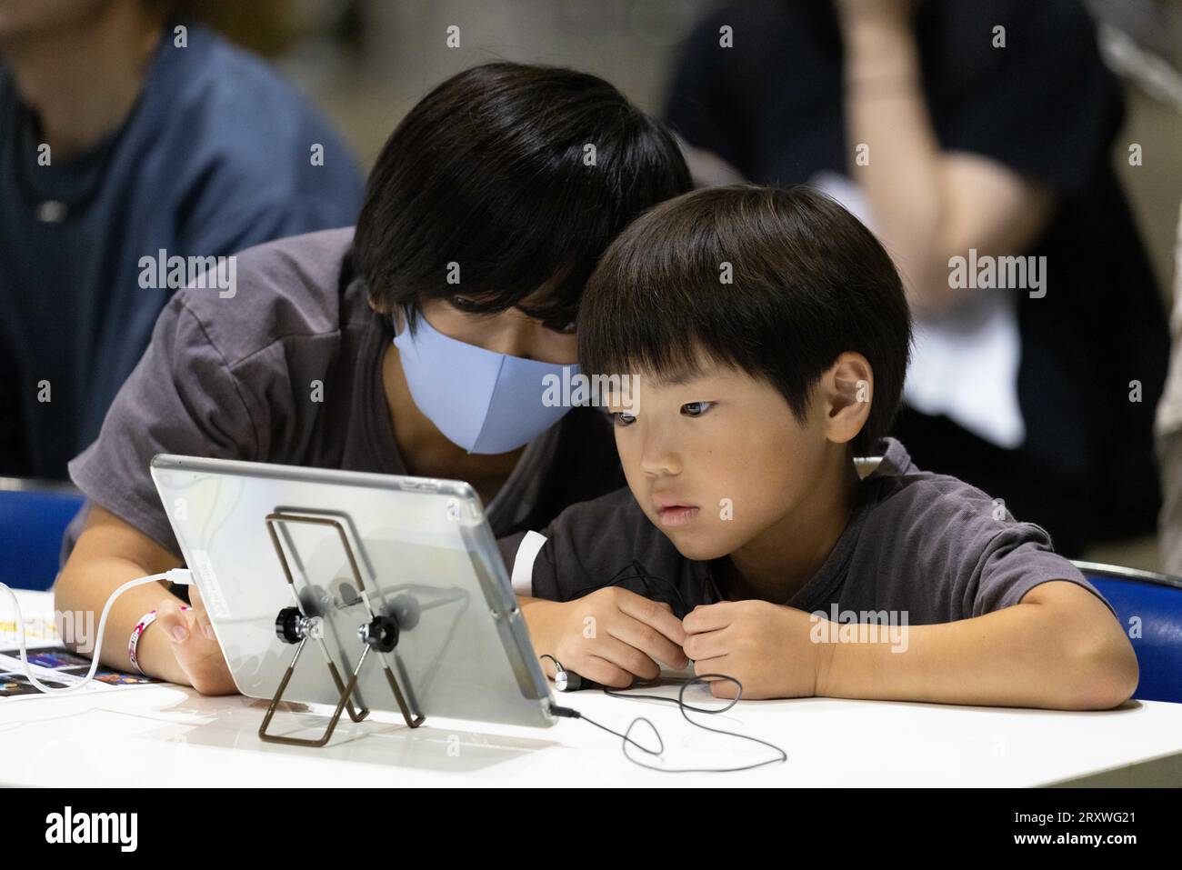 Participant of a video game programming workshop for kids receives help from an assistant inside ...