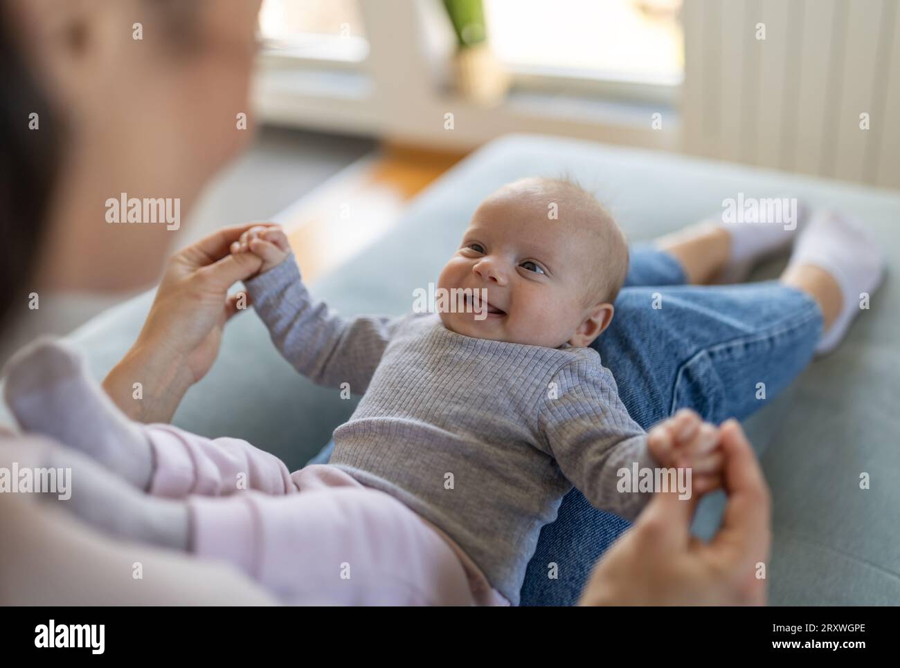 Young mother sitting on sofa at home and holding cute smiling newborn ...