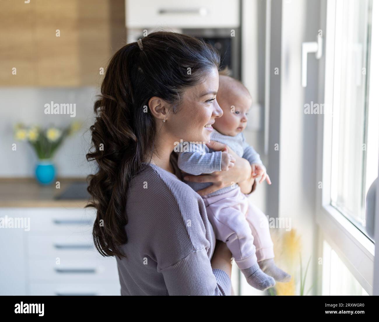Smiling pretty mum holding infant in arms and enjoying tender moment at ...