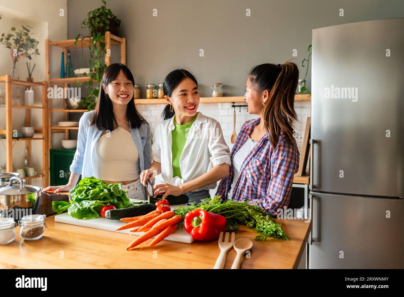 Happy beautiful chinese women friends bonding at home and cooking ...