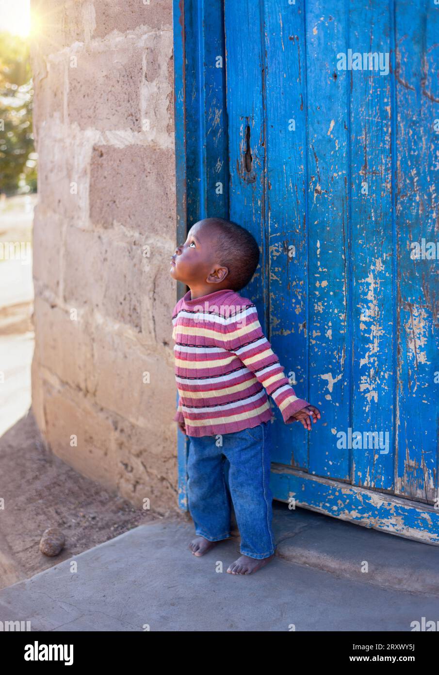 african child standing in front of the door of his house in the village ...