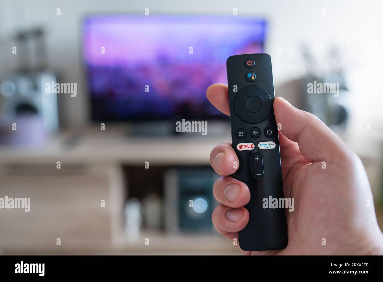 A woman's hand holds a TV remote control, on which there are buttons ...