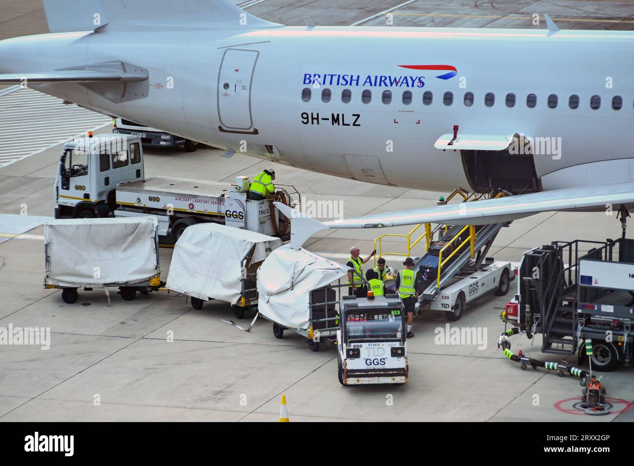 London, England, UK - 1 August 2023: Airport workers unloading luggage ...