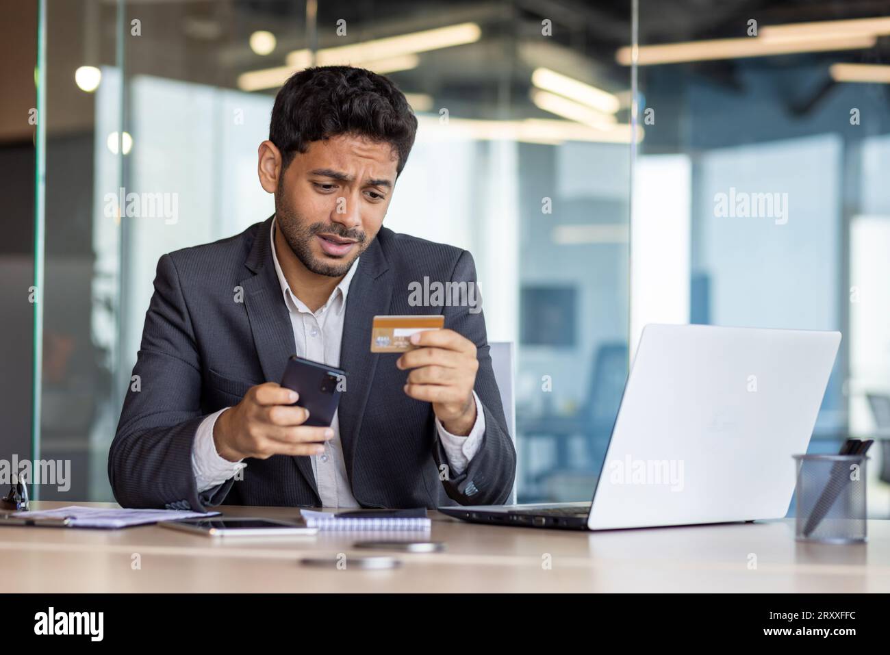 Upset young male office worker sitting at desk and holding phone and ...