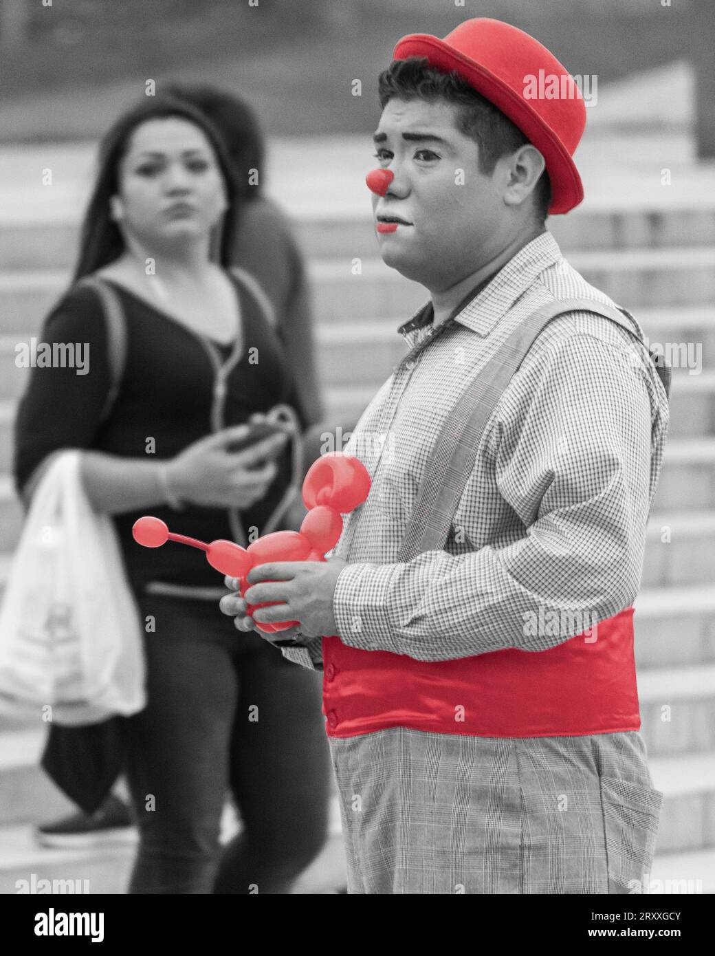 A clown shapes a balloon figure, but their sad and contemplative gaze ...