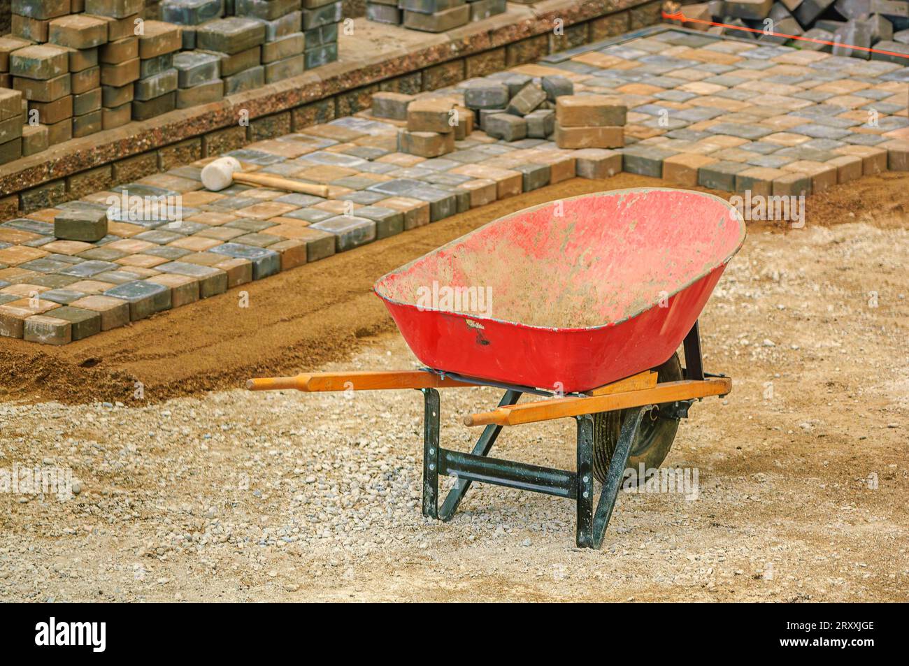 A red wheel barrow next to stacks of paving bricks at a construction ...