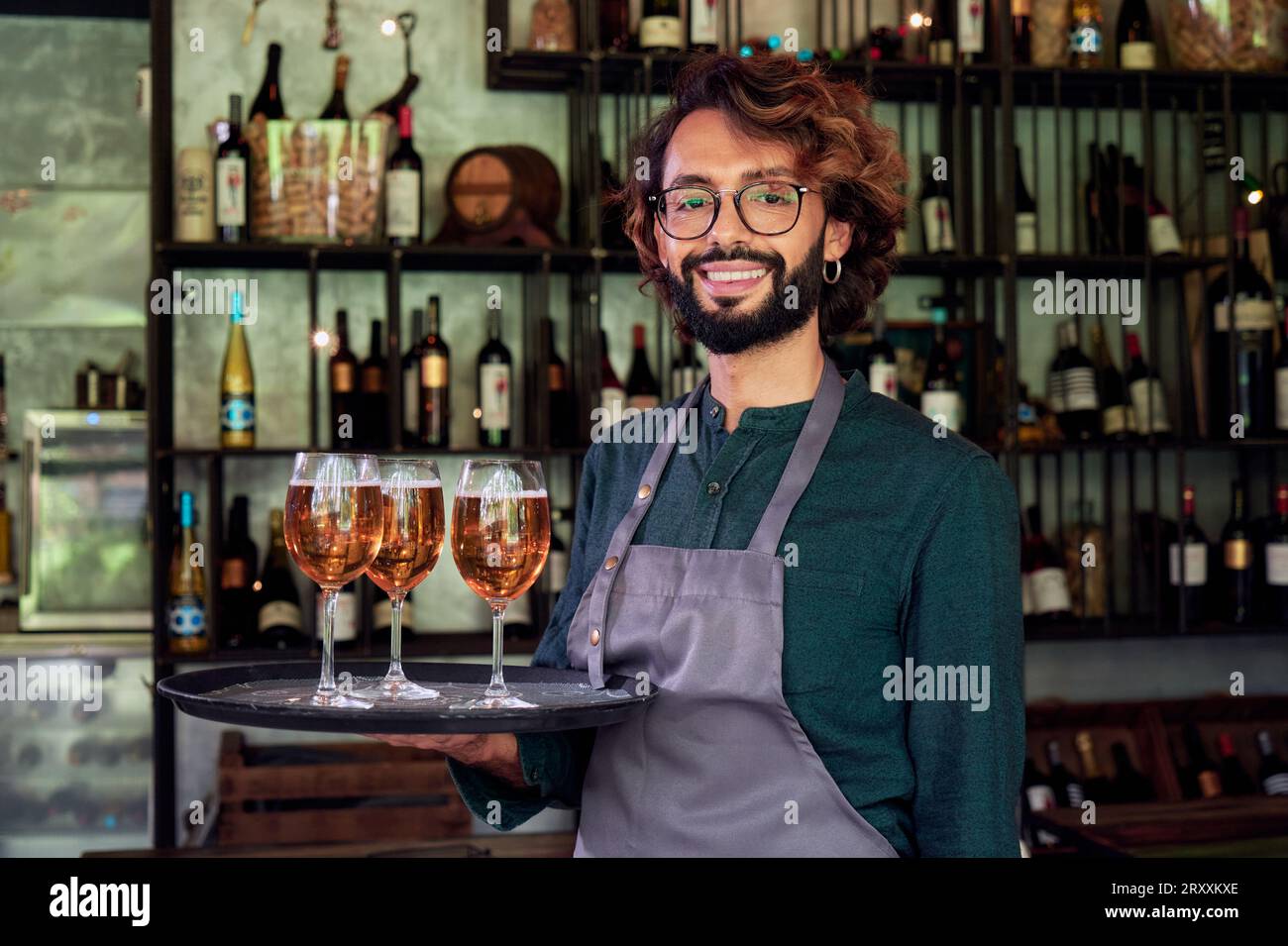 Front view of a cheerful waiter looking at camera smiling while holding ...