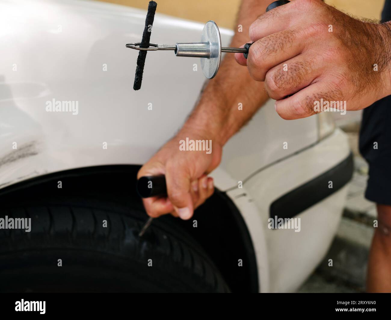 Concept: automobile mechanics. Hands enlarging a puncture in a tire to ...