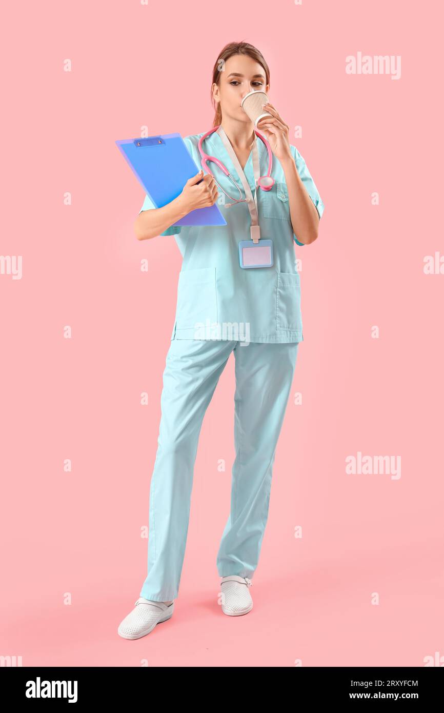 Female medical intern with clipboard drinking coffee on pink background ...