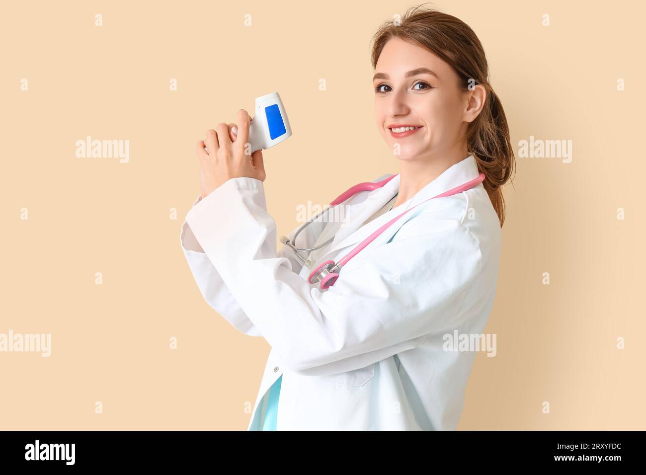 Female medical intern with infrared thermometer on beige background ...