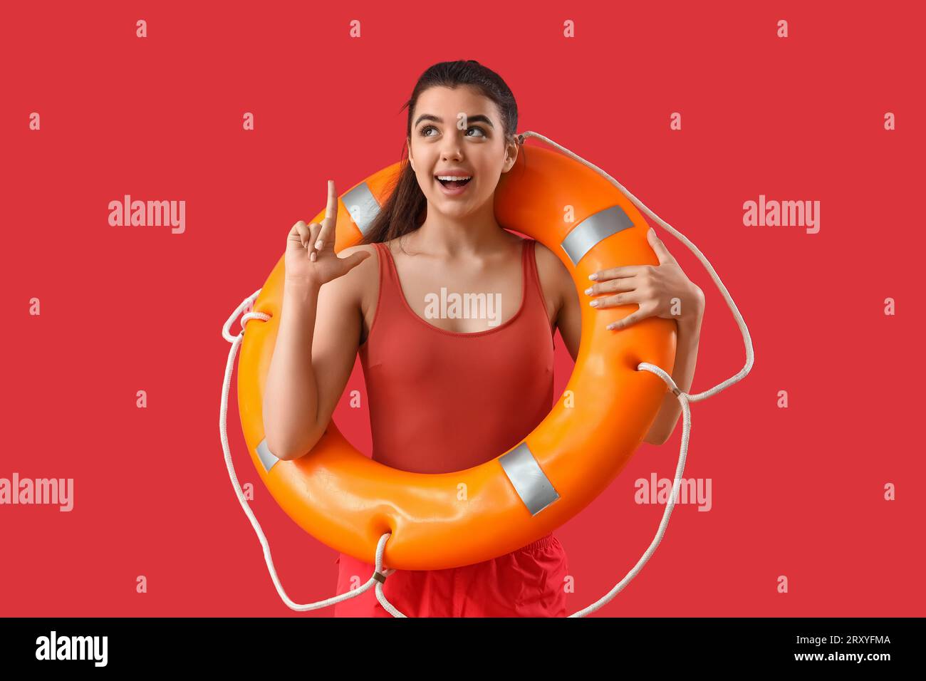 Female lifeguard with ring buoy pointing at something on red background ...