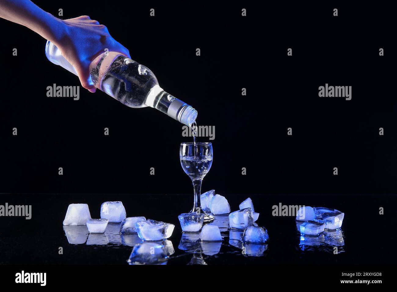 Woman pouring cold vodka from bottle into shot on black background ...