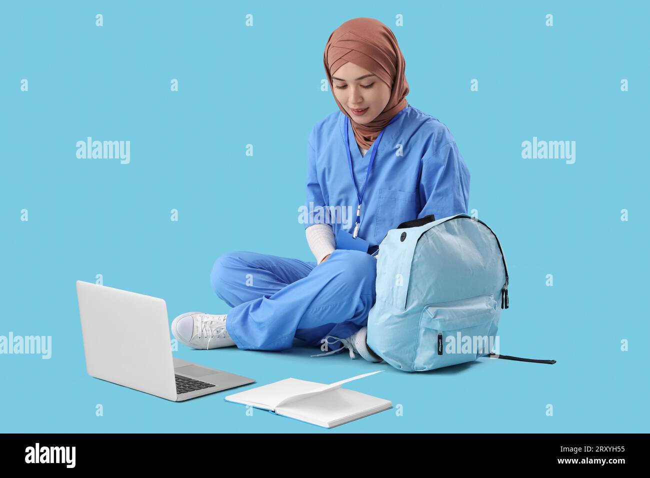 Female Muslim medical intern with backpack studying on blue background ...