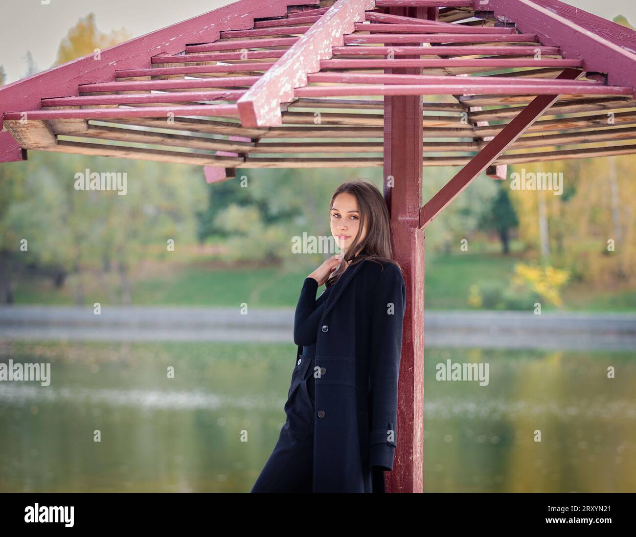 A beautiful girl poses while standing by a pond under an umbrella in an ...