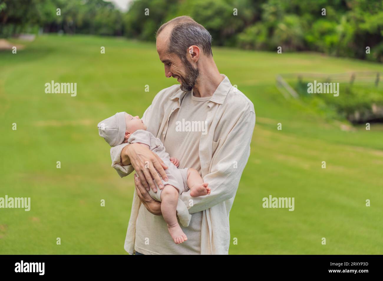 A happy 40-year-old father cradles her newborn in a sun-drenched park ...