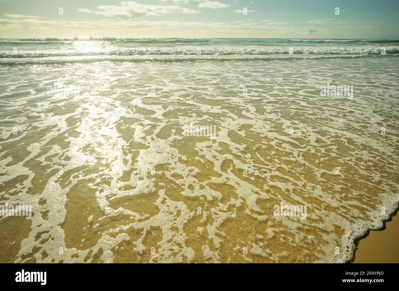 Foamy white wash as waves break and roll across the sandy beach. Empty ...
