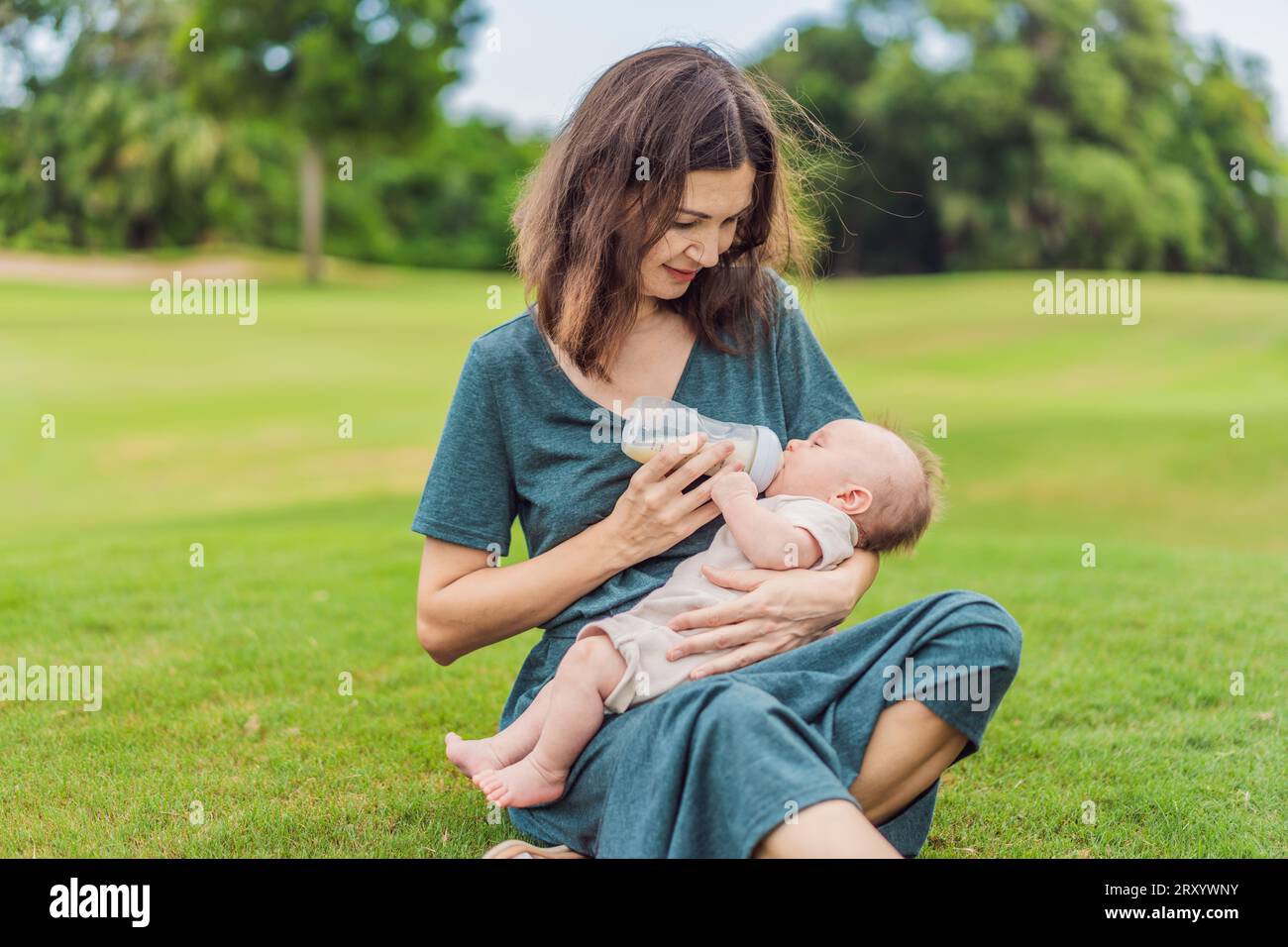 Mother holding and feeding baby from milk bottle in the park. Portrait ...