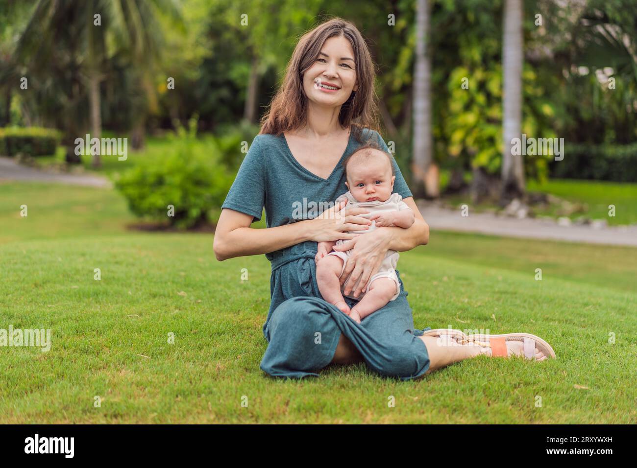 A happy 40-year-old mother cradles her newborn in a sun-drenched park ...
