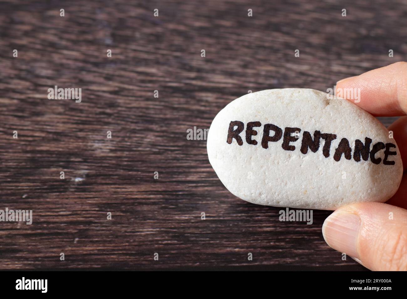 Hand-holding rock with handwritten word "repentance" over a wooden ...