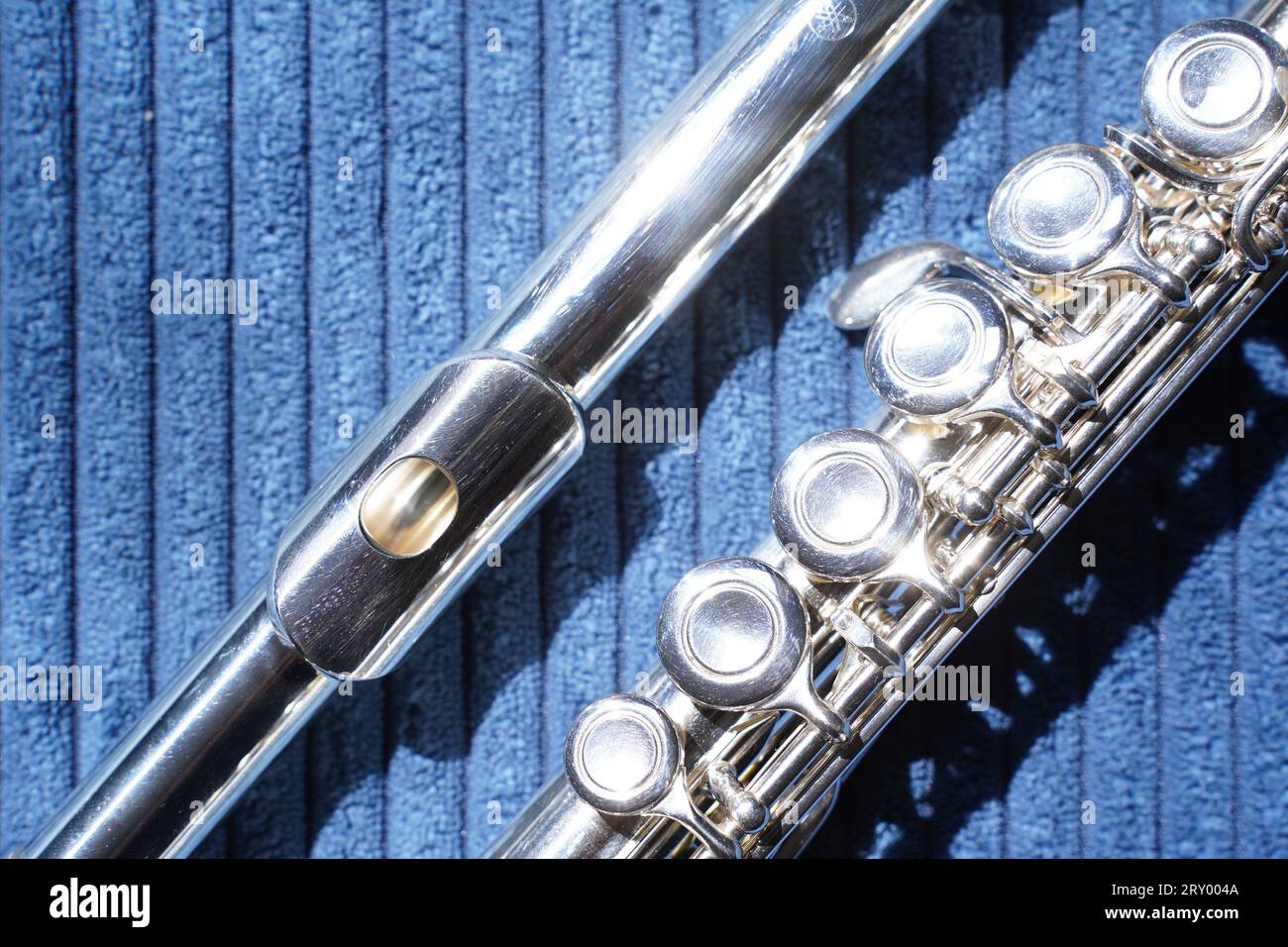 A silver flute lies glistening in the sun on a blue background. Musical ...