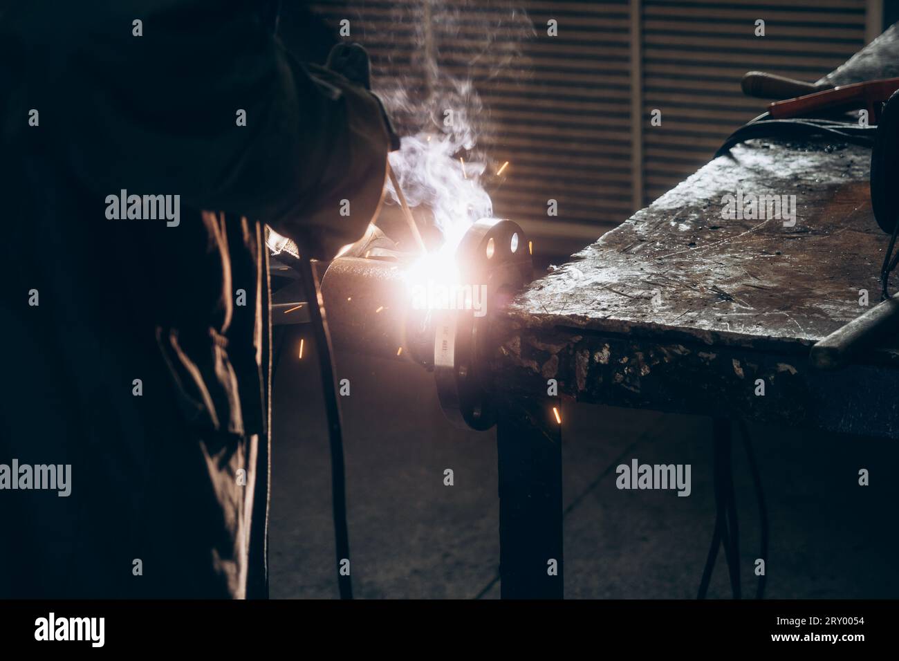 Welder works at workbench in welding shop. Flash. Electric arc. Dark ...