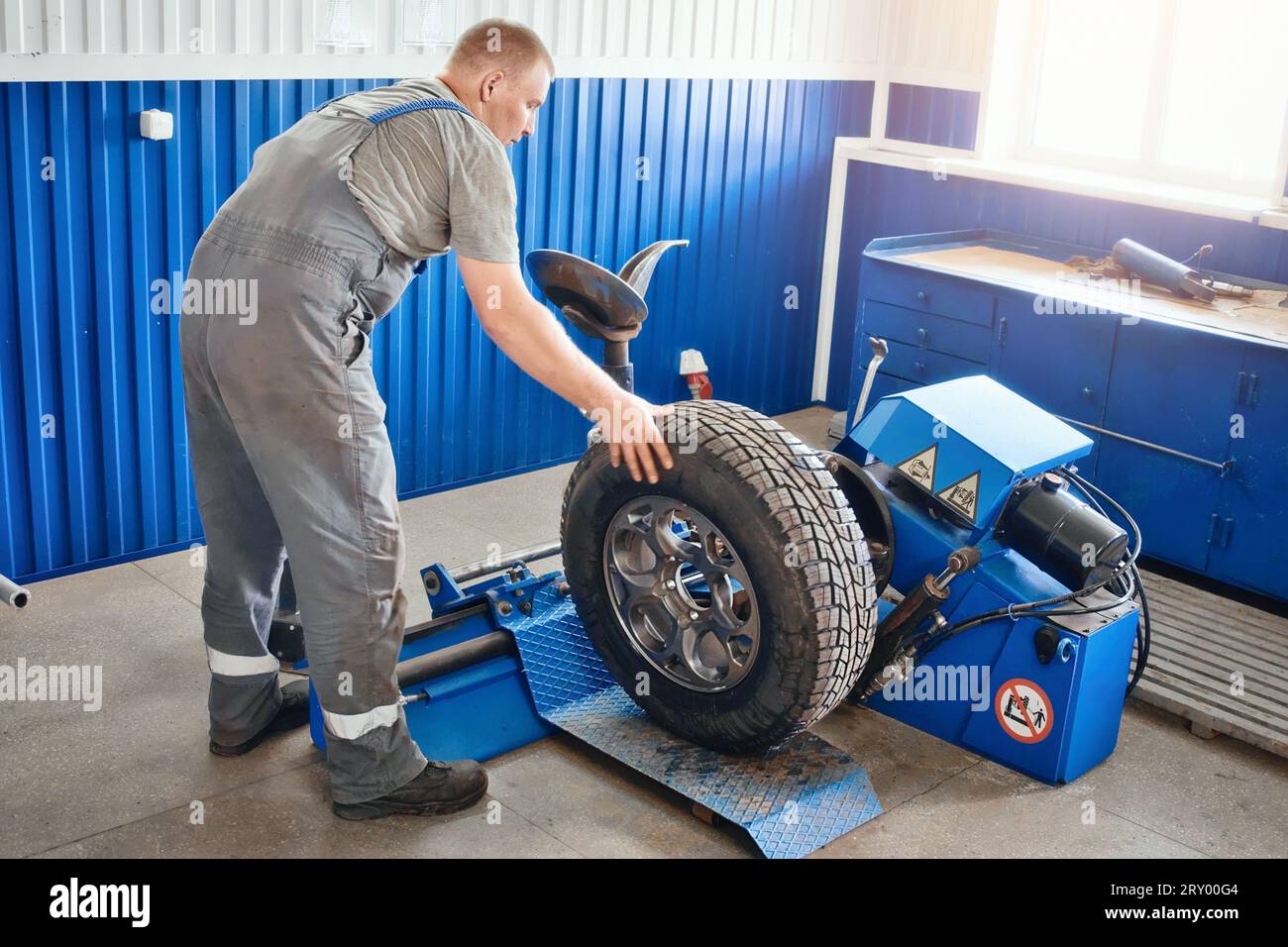 Mechanic works in tire repair shop. Car service mechanic puts wheel on ...
