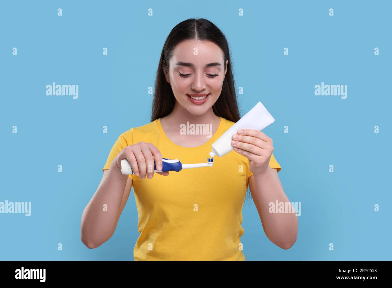 Happy young woman squeezing toothpaste from tube onto electric ...