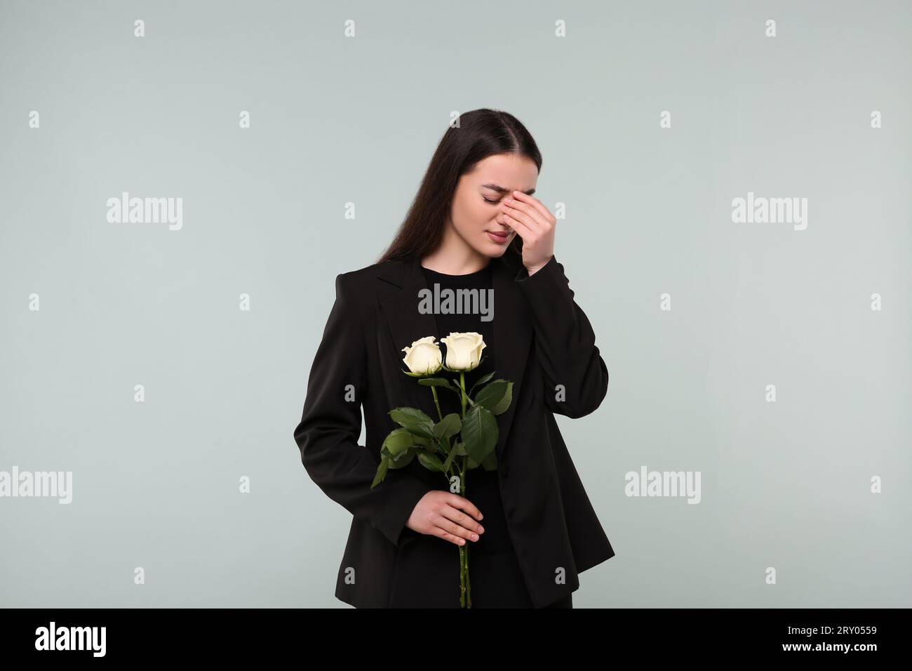 Sad woman with white rose flowers mourning on light grey background ...