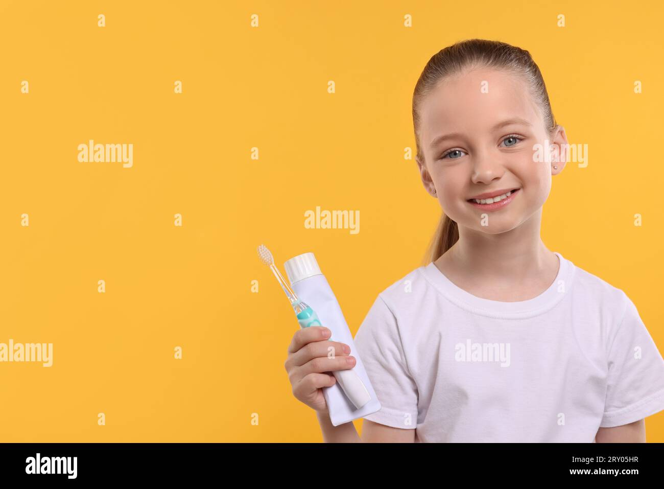 Happy girl holding electric toothbrush and tube of toothpaste on yellow ...