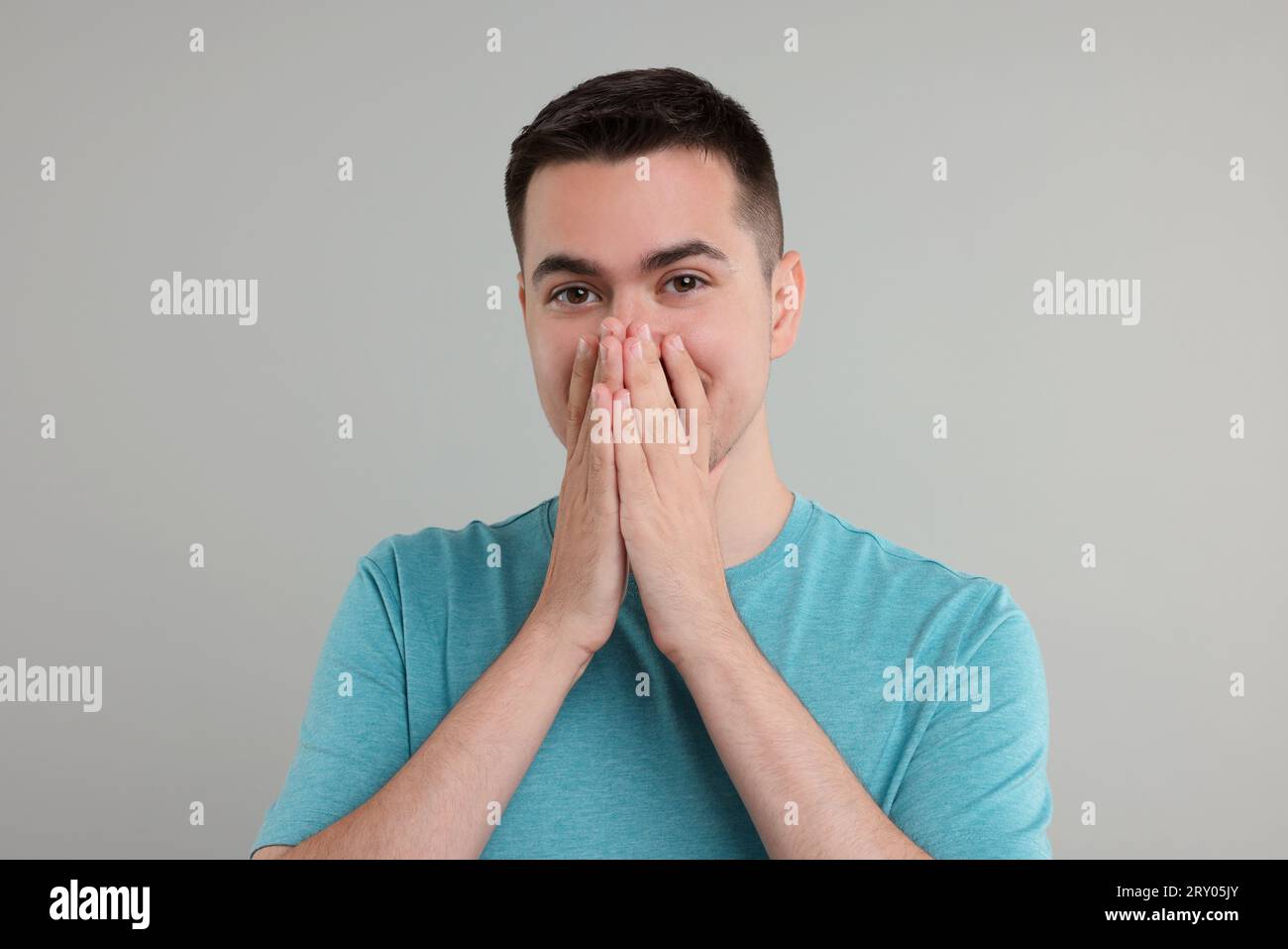 Embarrassed man covering mouth with hands on grey background Stock ...