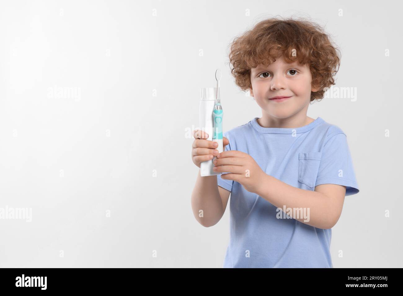 Cute little boy holding electric toothbrush and tube of toothpaste on ...