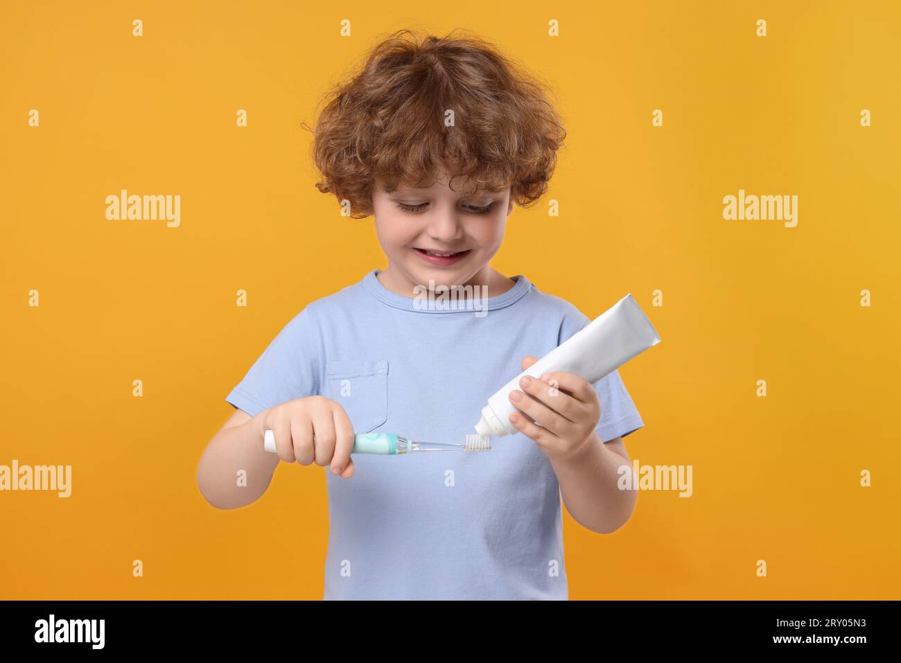 Cute little boy squeezing toothpaste from tube onto electric toothbrush ...