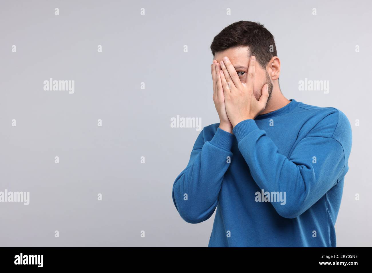 Embarrassed man covering face on light grey background. Space for text ...