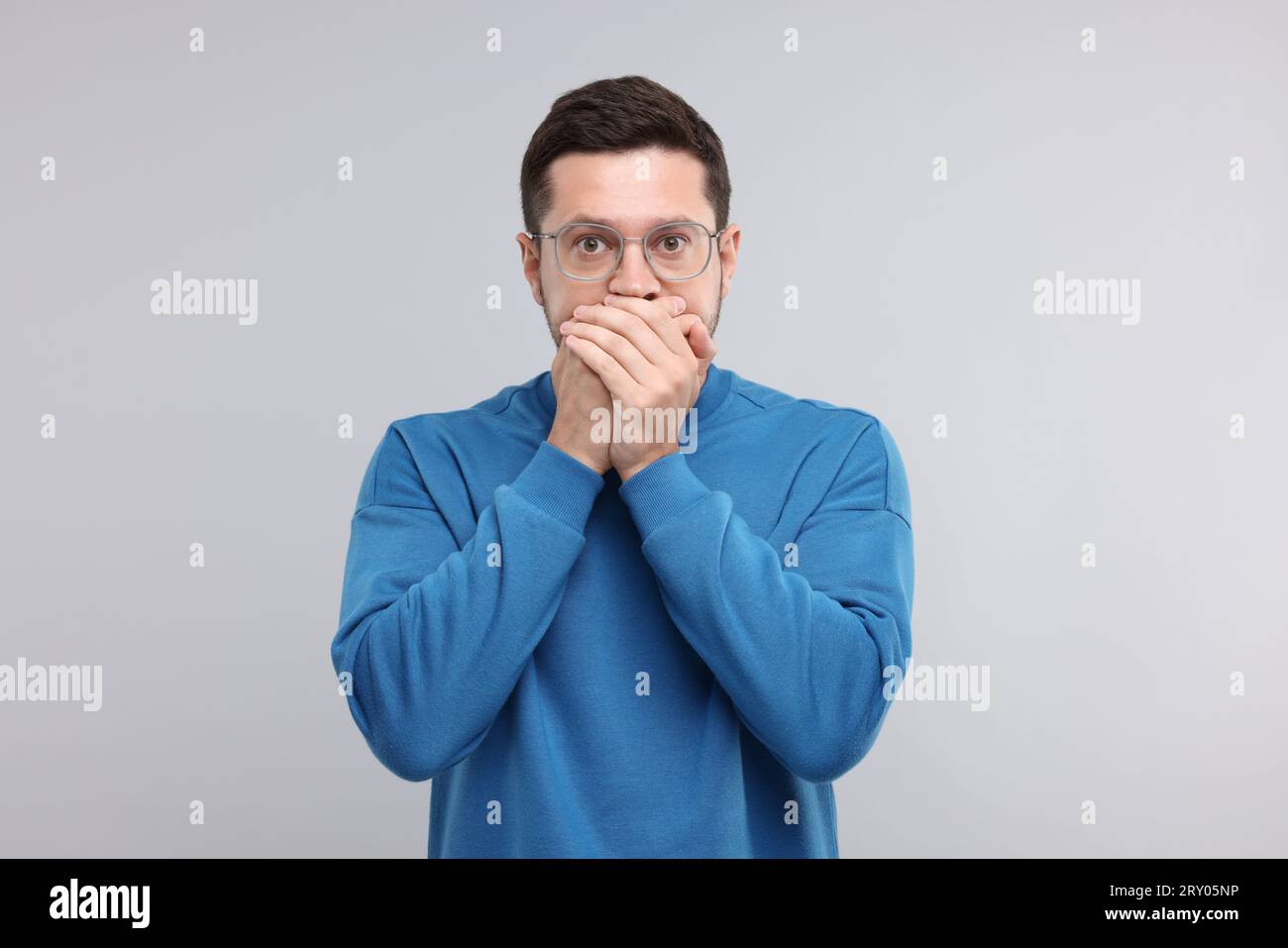 Embarrassed man covering mouth on light grey background Stock Photo - Alamy