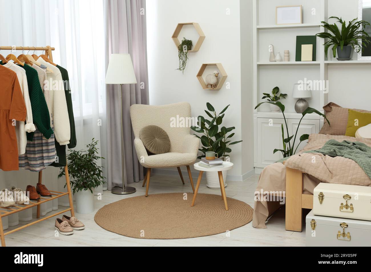 Stylish bedroom with comfortable bed, clothes rack and different ...
