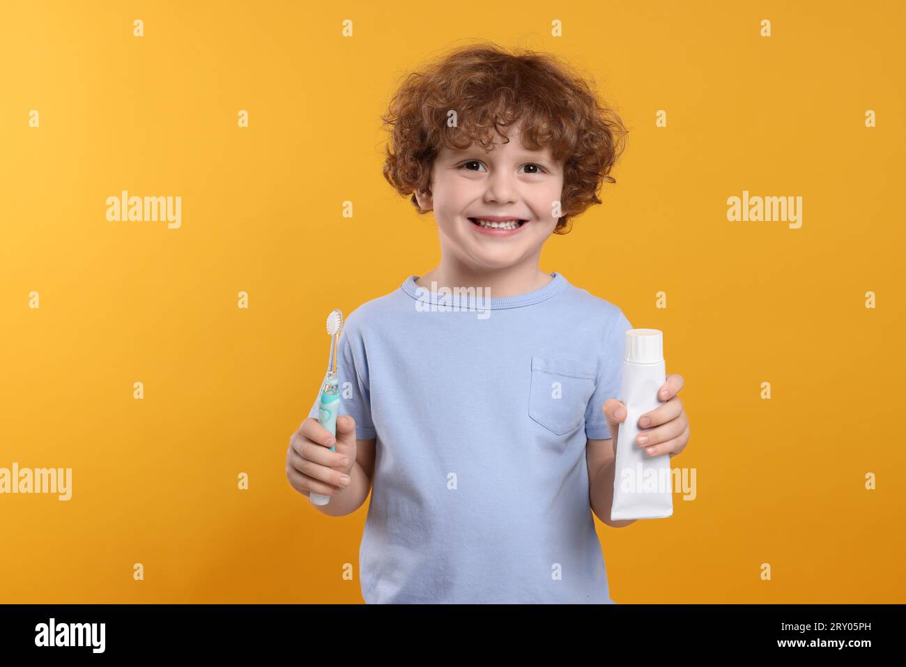 Cute little boy holding electric toothbrush and tube of toothpaste on ...