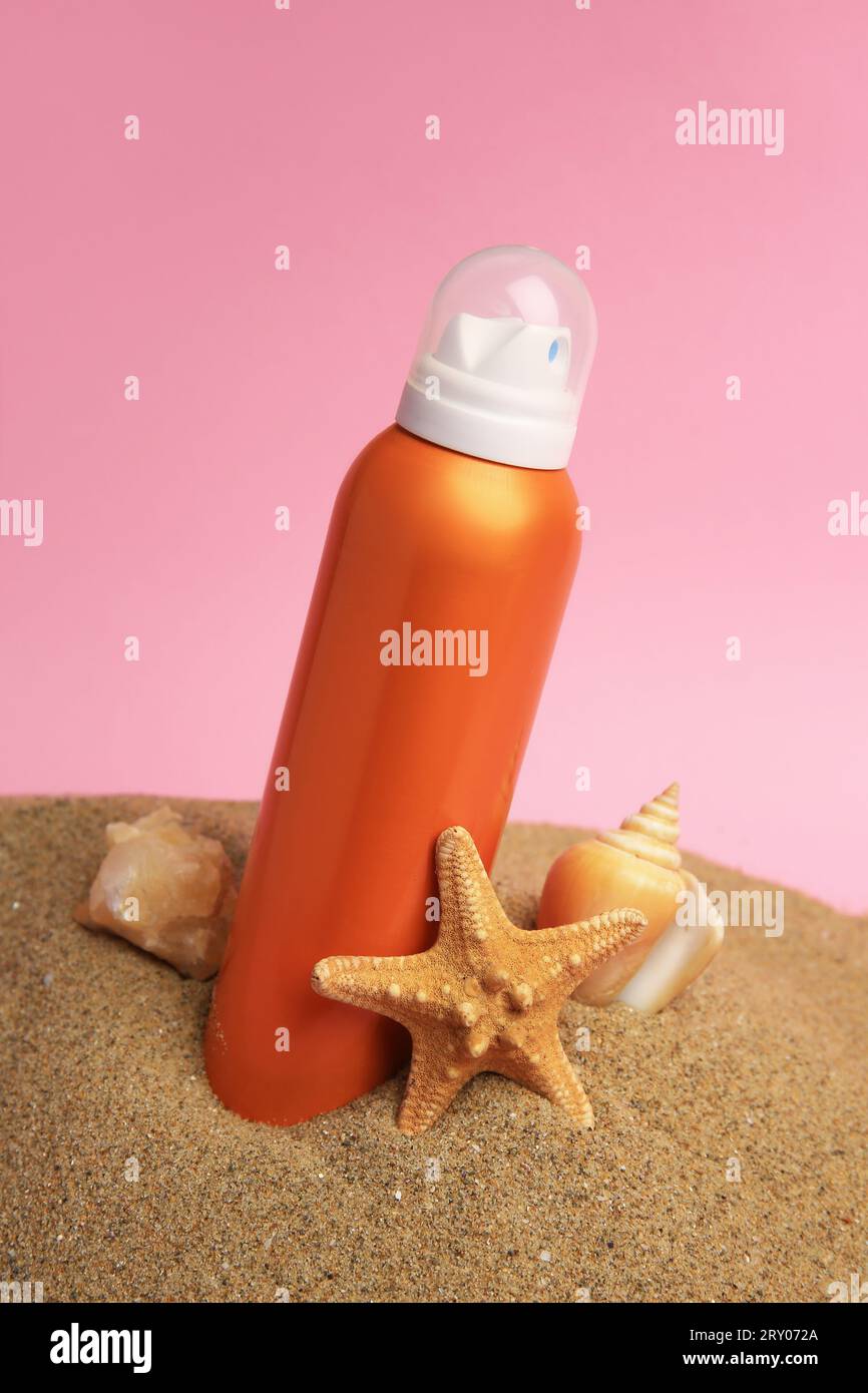 Sand with sunscreen, stone, starfish and seashell against pink ...