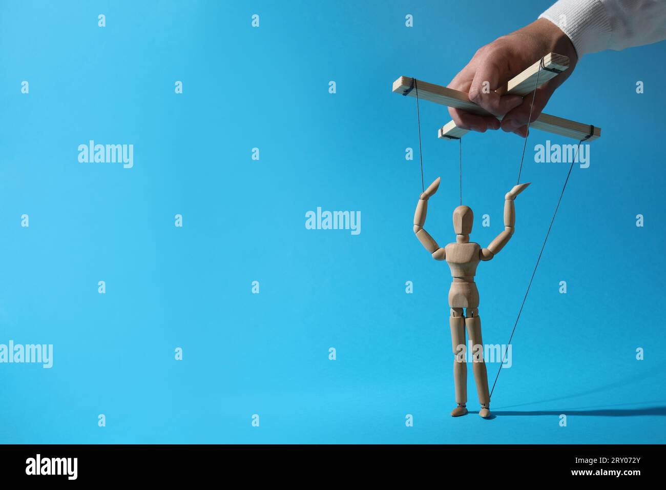 Man pulling strings of puppet on light blue background, closeup. Space ...