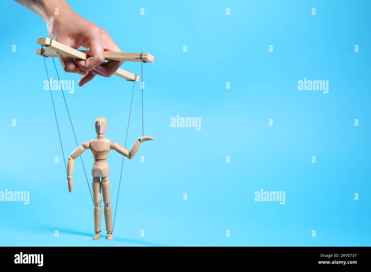 Man pulling strings of puppet on light blue background, closeup. Space ...