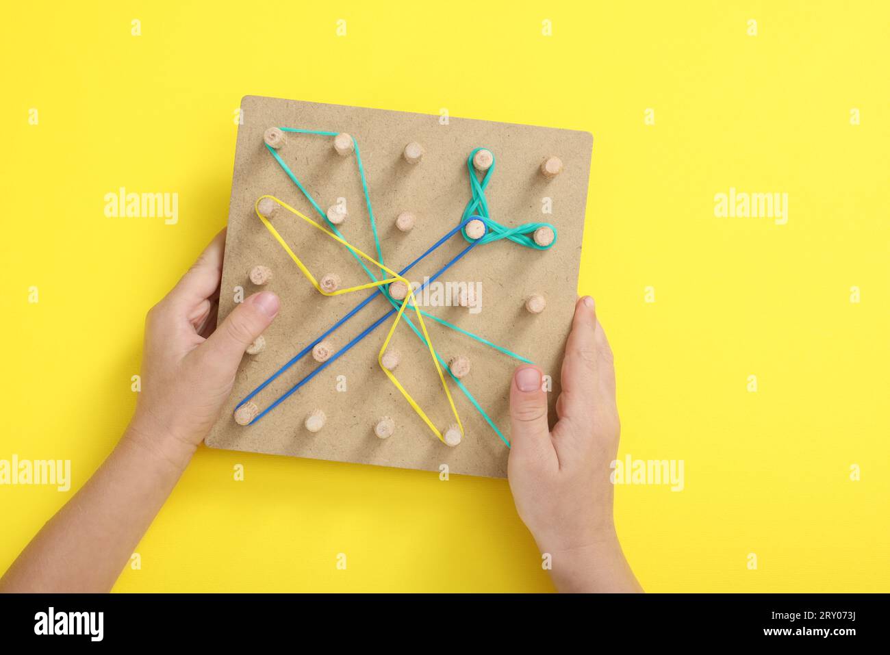 Motor skills development. Boy with geoboard and rubber bands at yellow ...