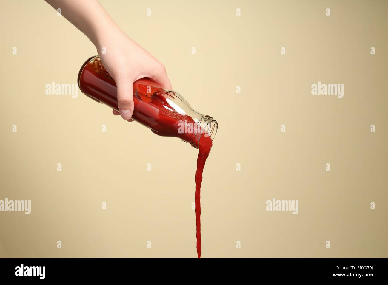 Woman pouring tasty ketchup from bottle on beige background, closeup ...