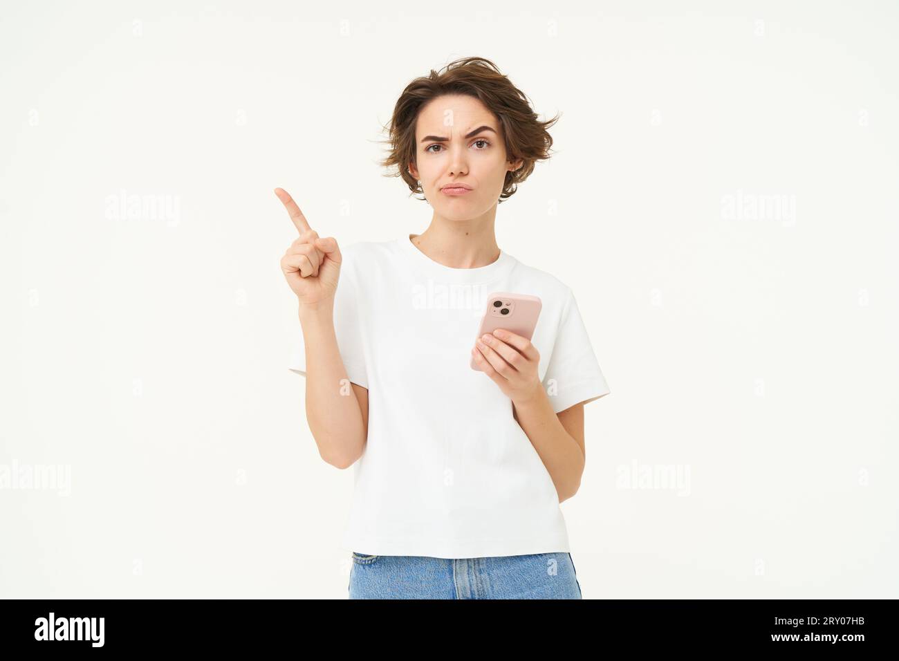 Portrait of woman with smartphone, looking puzzled and pouting ...