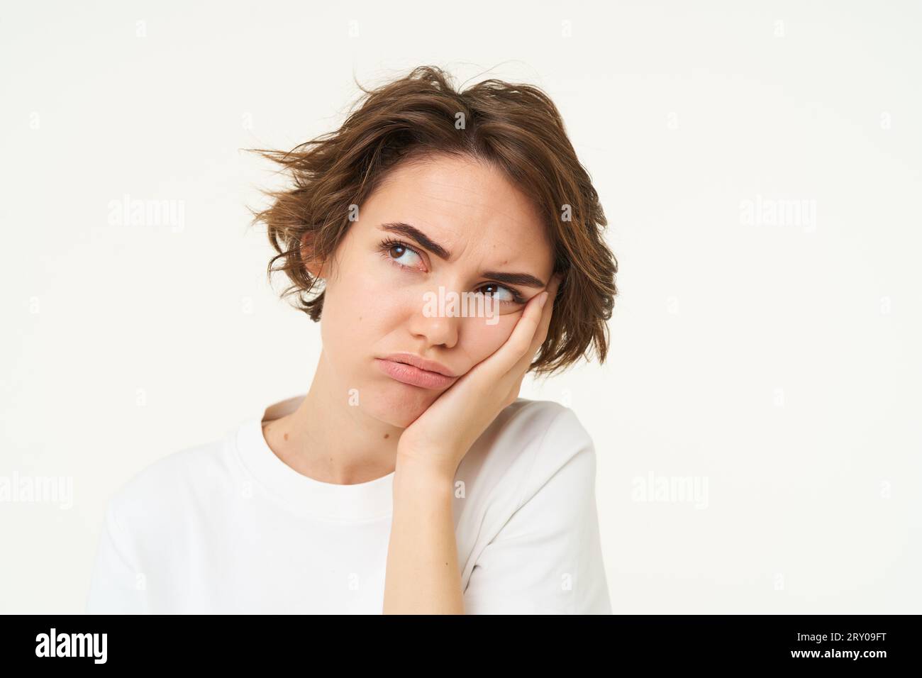 Portrait of young bored woman, leans head on hand and frowns, looks ...