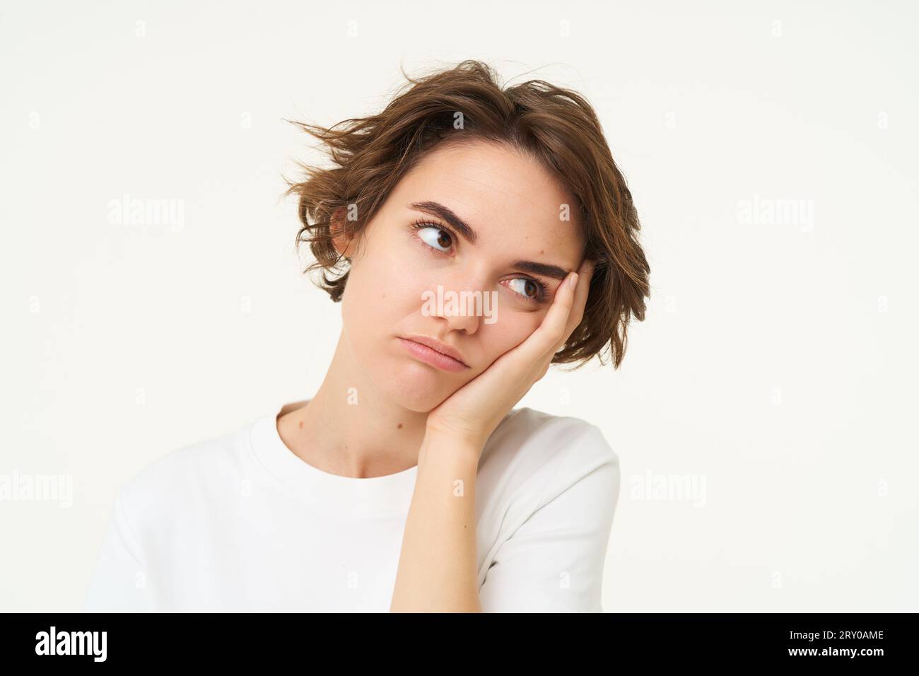 Portrait of young bored woman, leans head on hand and frowns, looks ...