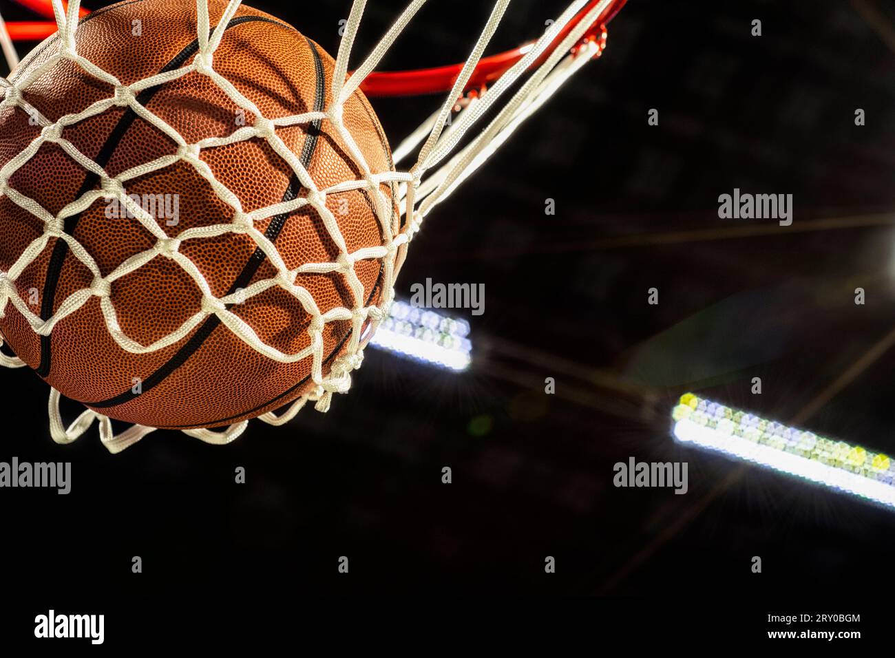 A close-up view looking up at an orange basketball falling through the ...