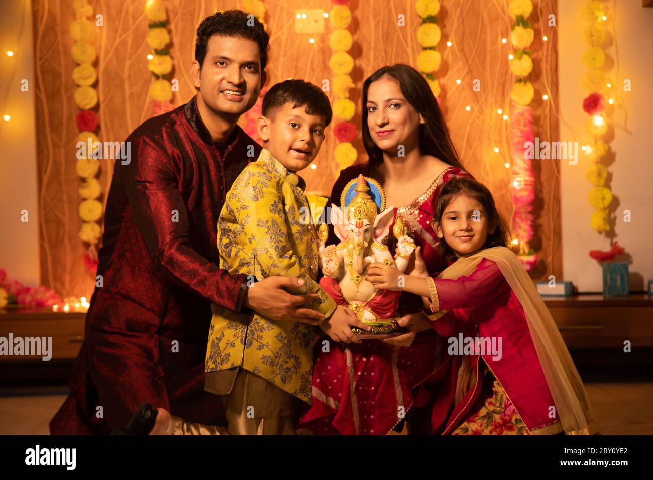 Happy young Indian family in traditional dress holding Ganesh idol or ...